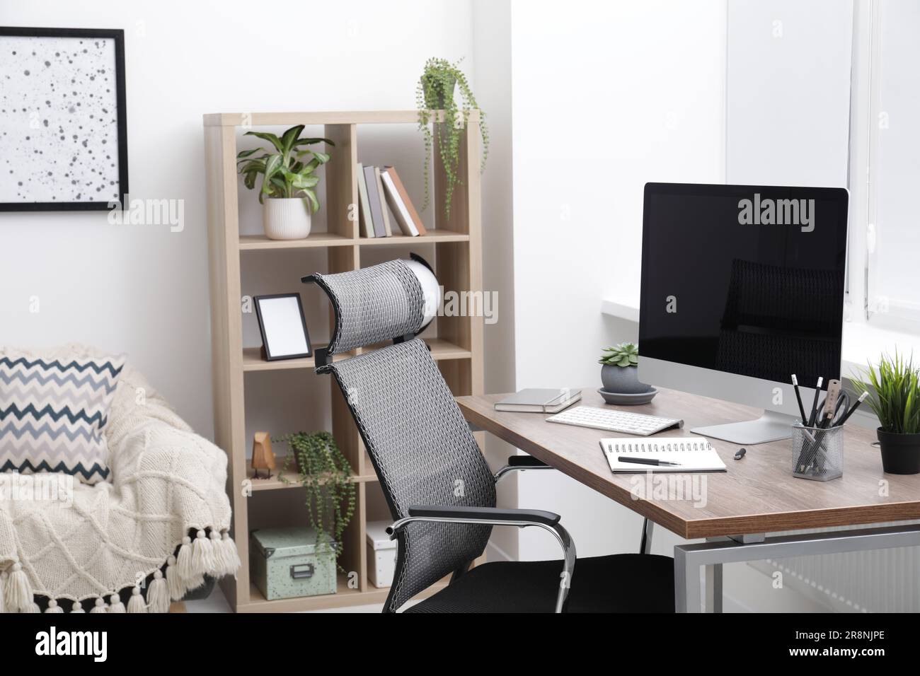 Cosy workspace with computer on desk, stylish furniture and potted ...