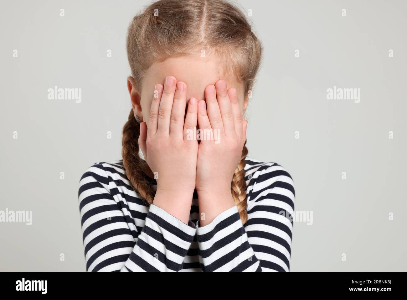 Girl covering face with hands on light grey background. Children's ...