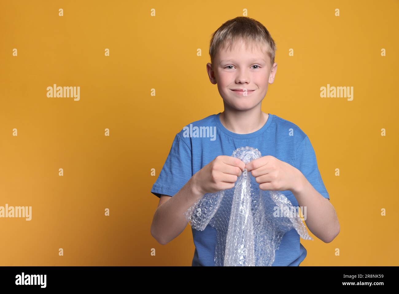 Boy popping bubble wrap on yellow background, space for text. Stress ...