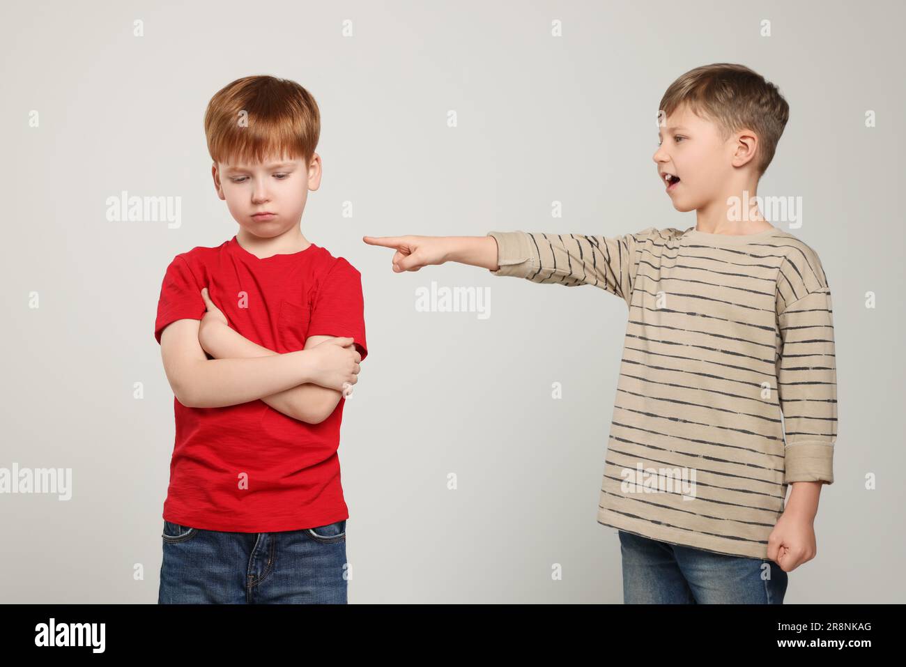 Boy laughing and pointing at upset kid on light grey background ...