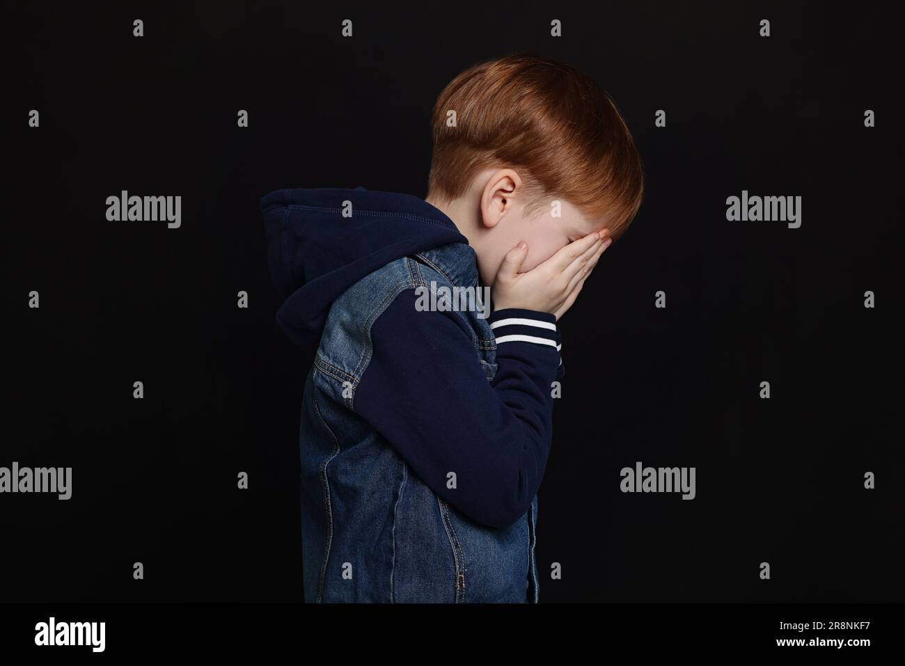 Boy covering face with hands on black background. Children's bullying ...