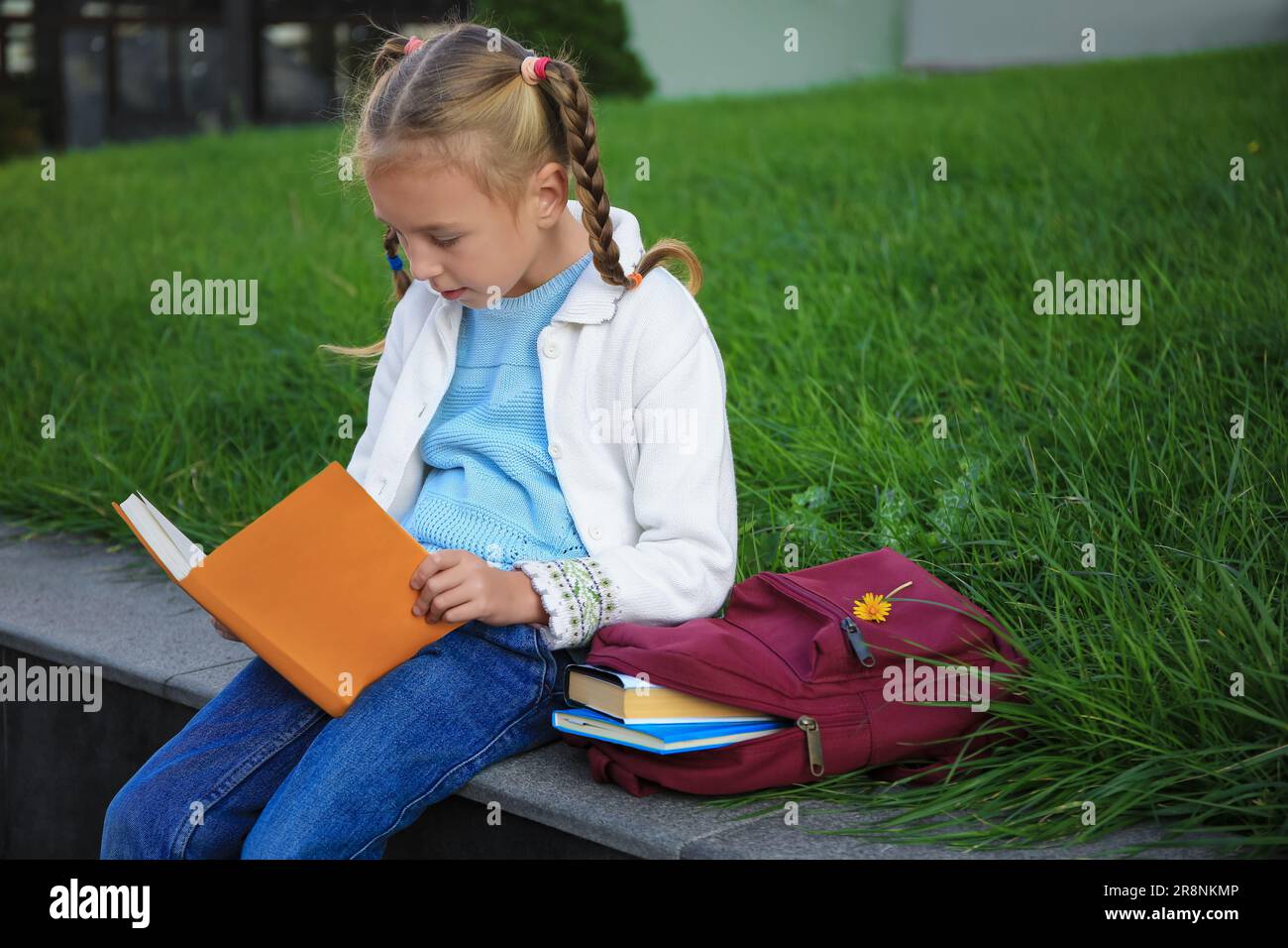 Cute little girl with backpack reading textbook on city street. Space ...