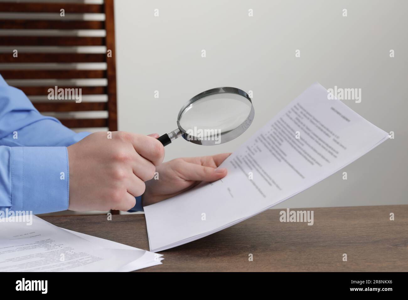 Man looking at document through magnifier at wooden table, closeup ...