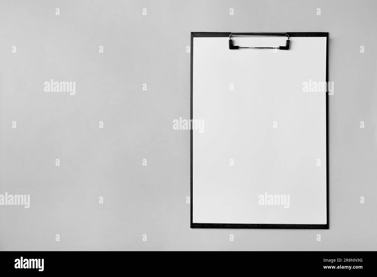Black clipboard with sheet of blank paper on light grey background, top ...