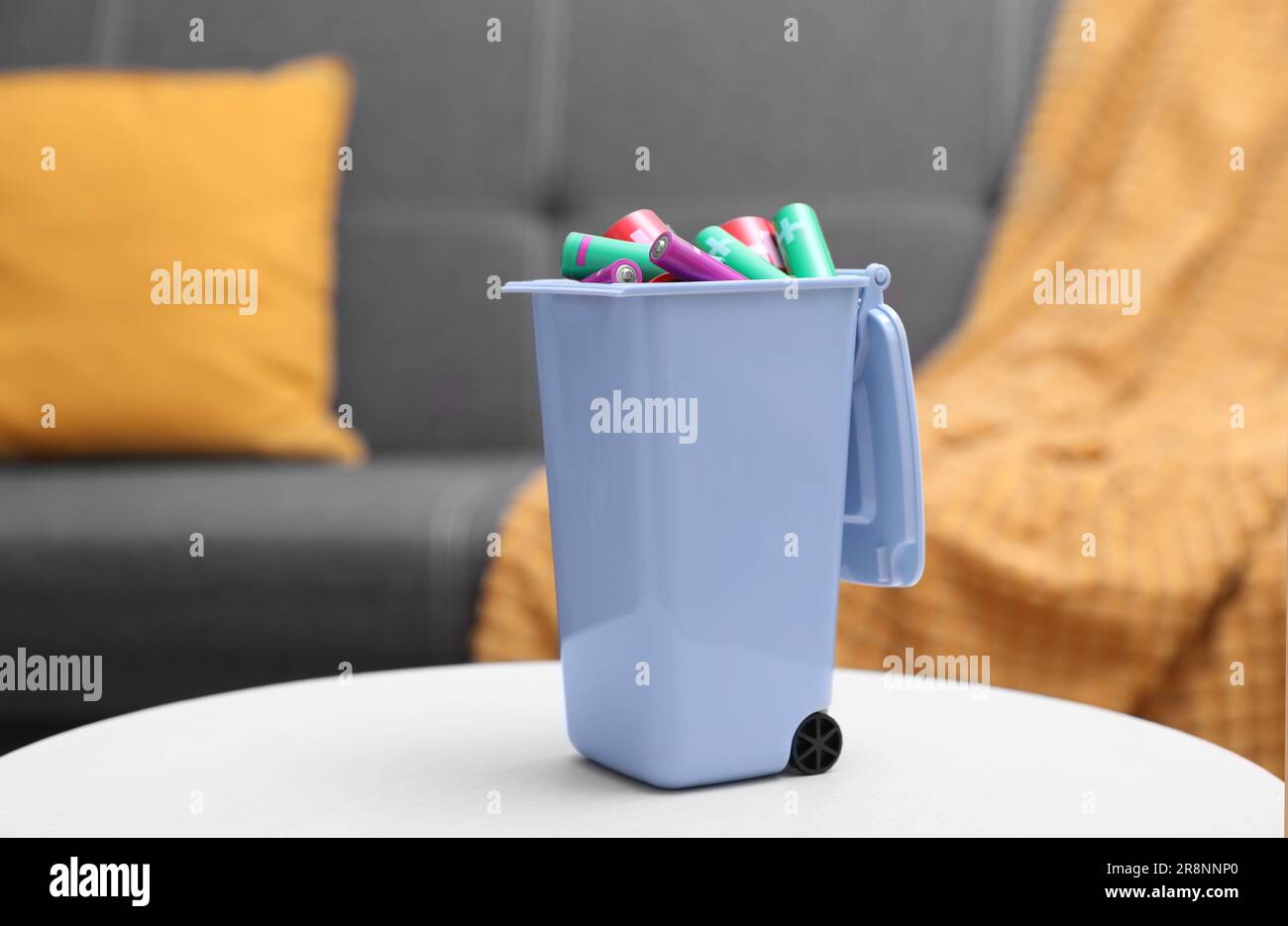 Mini recycling bin with different types of batteries on white table ...