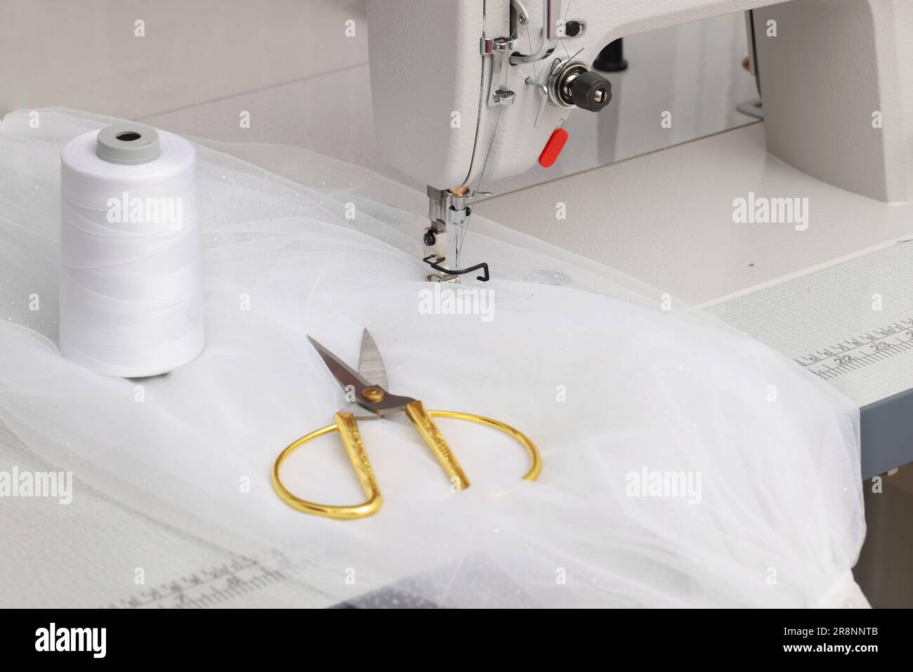 Sewing machine with white fabric, scissors and threads on table ...