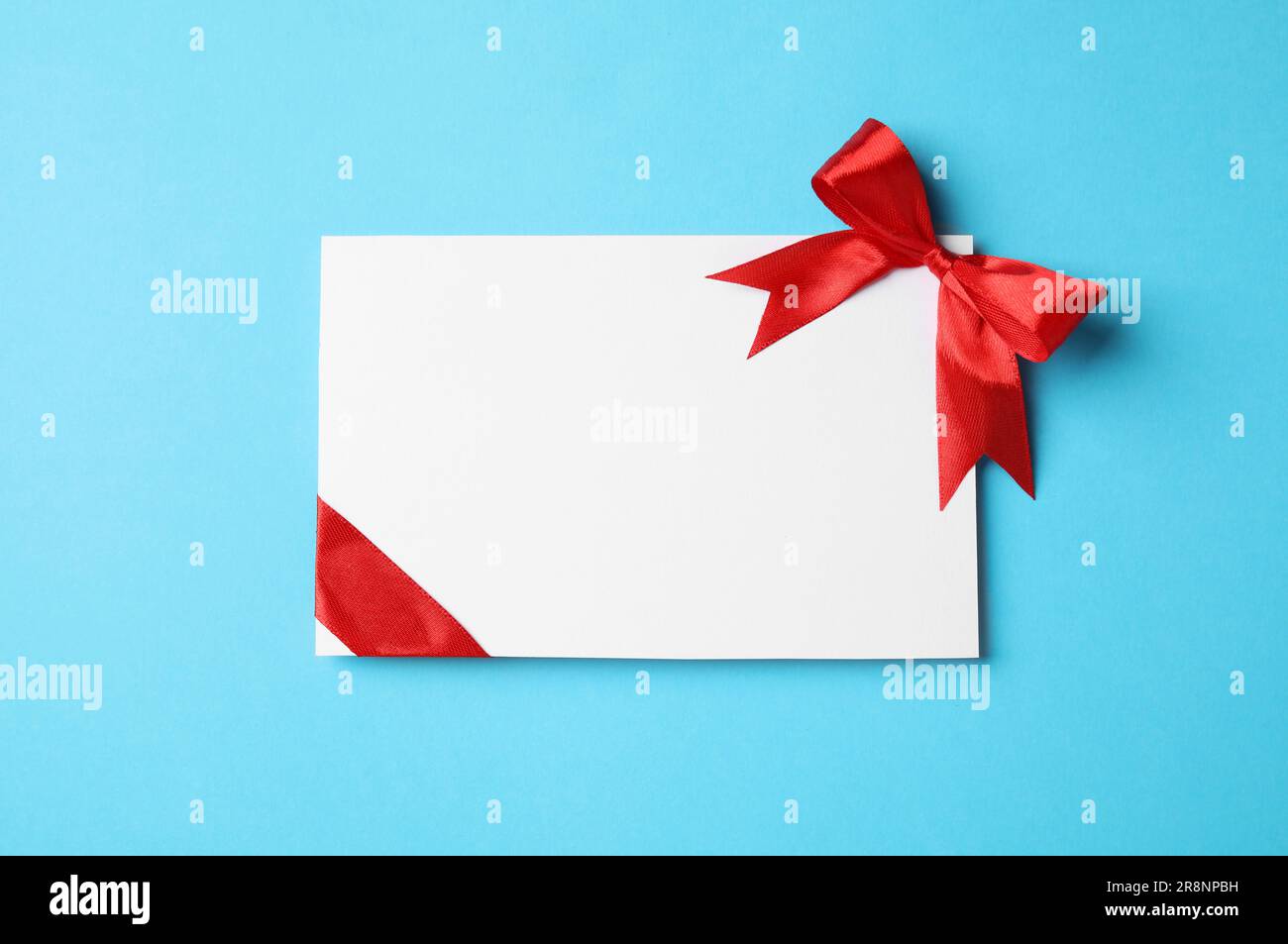 Blank gift card with red bow on light blue background, top view. Space ...