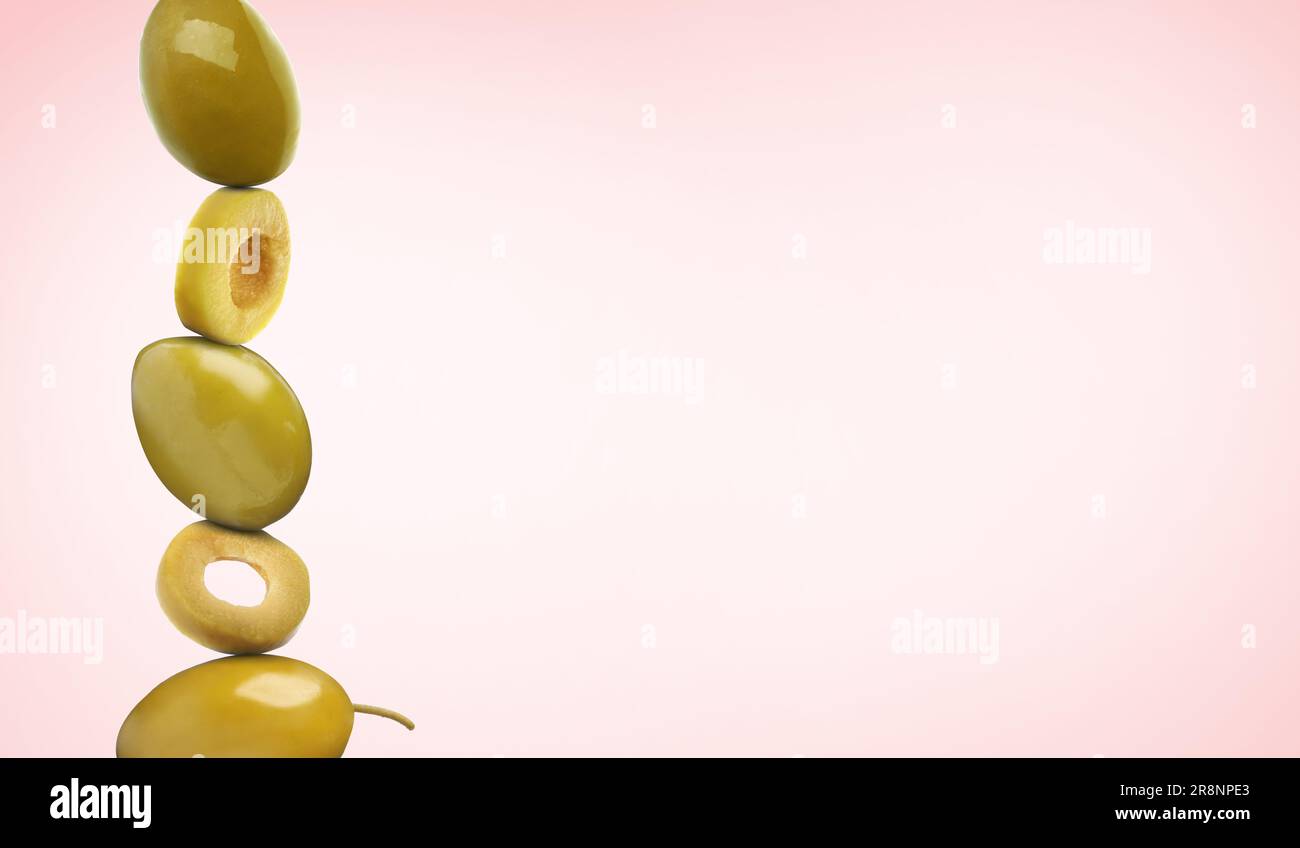 Cut and whole green olives on pink gradient background, space for text ...