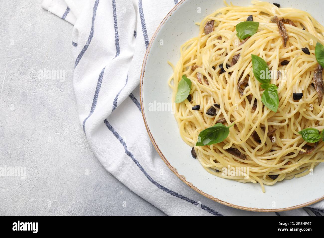 Delicious pasta with anchovies, olives and basil on light grey table ...