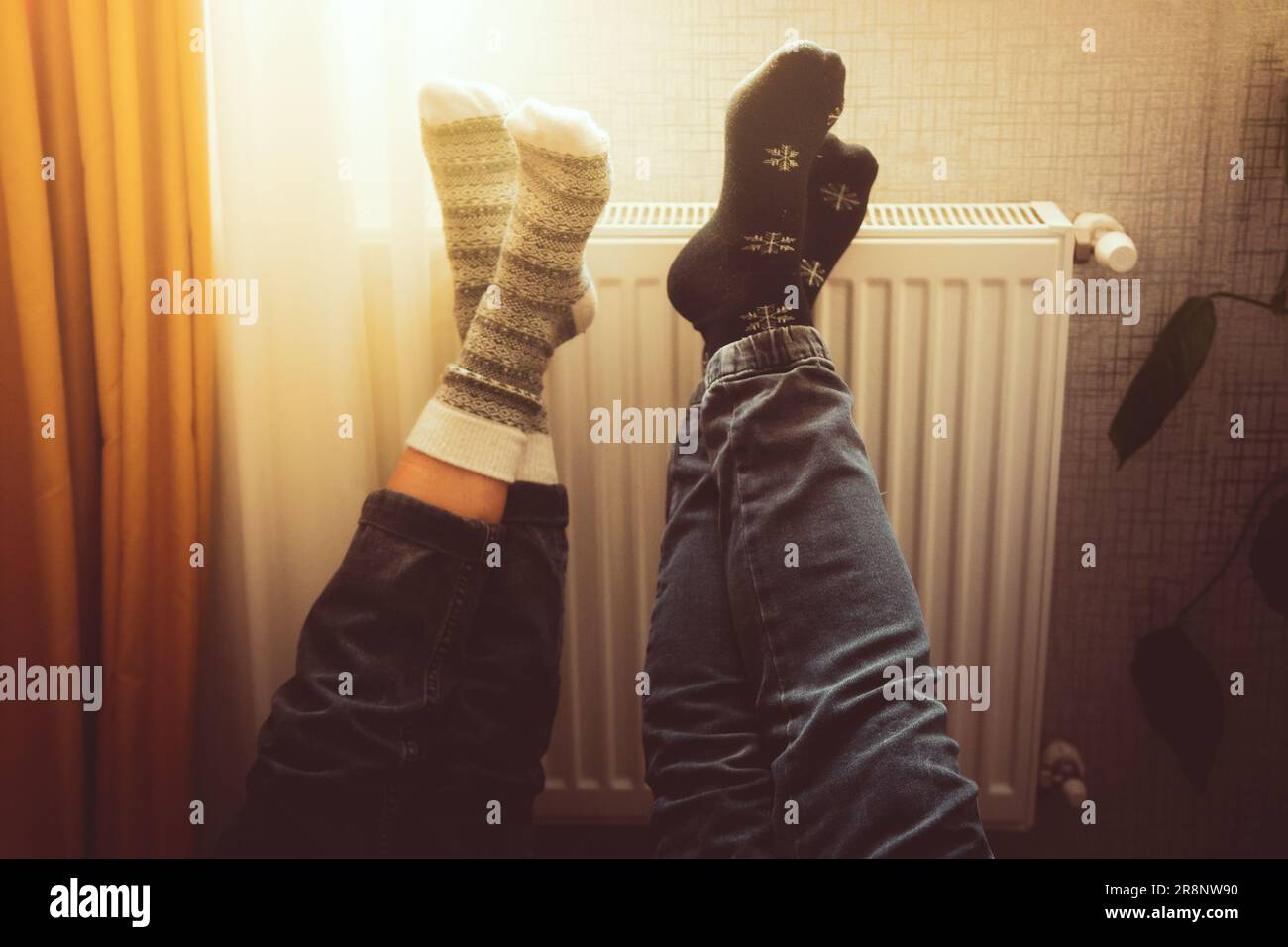 Couple hold legs up heating feet in cold home indoors on radiator in ...