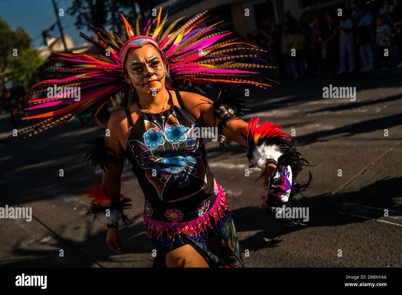 A young Mexican woman, wearing an Aztec feather headdress, performs a ...