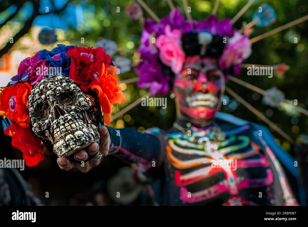A young Mexican woman, dressed as La Catrina, holds a Calavera statue ...
