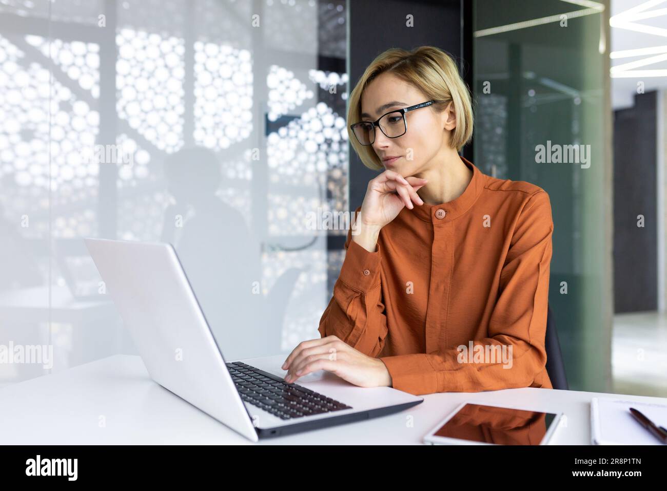 Serious thinking woman working with laptop inside office at workplace, businesswoman solving ...