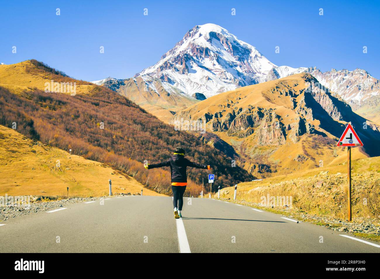 Female hiker run on road with scenic Kazbek mountain snowy peak ...