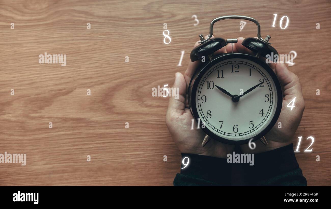 A hand holding vintage alarm clock with a flying numbers on wooden ...