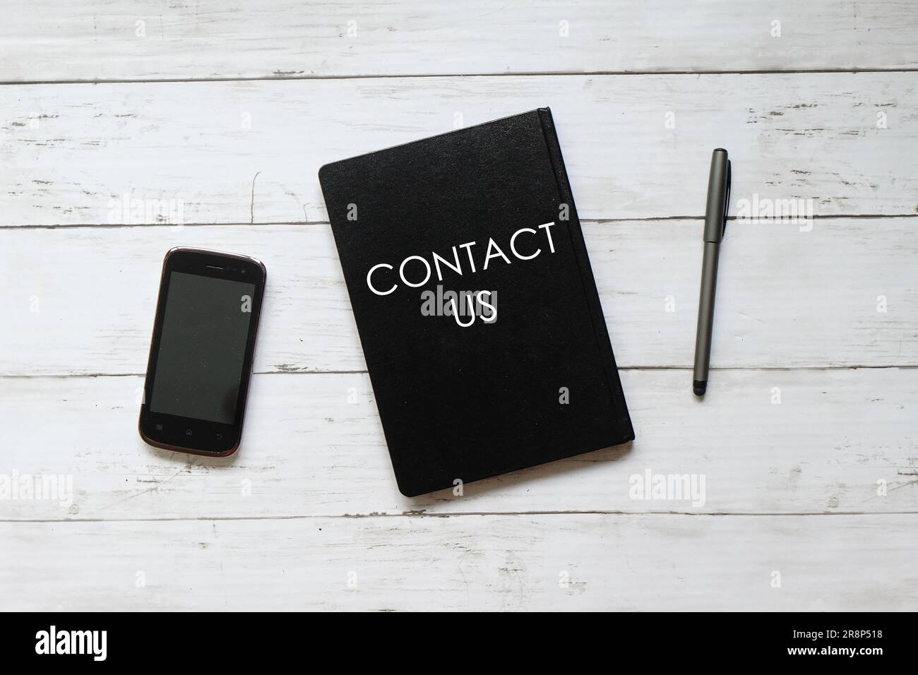 Top view mobile phone,pen and notebook written with CONTACT US on white ...