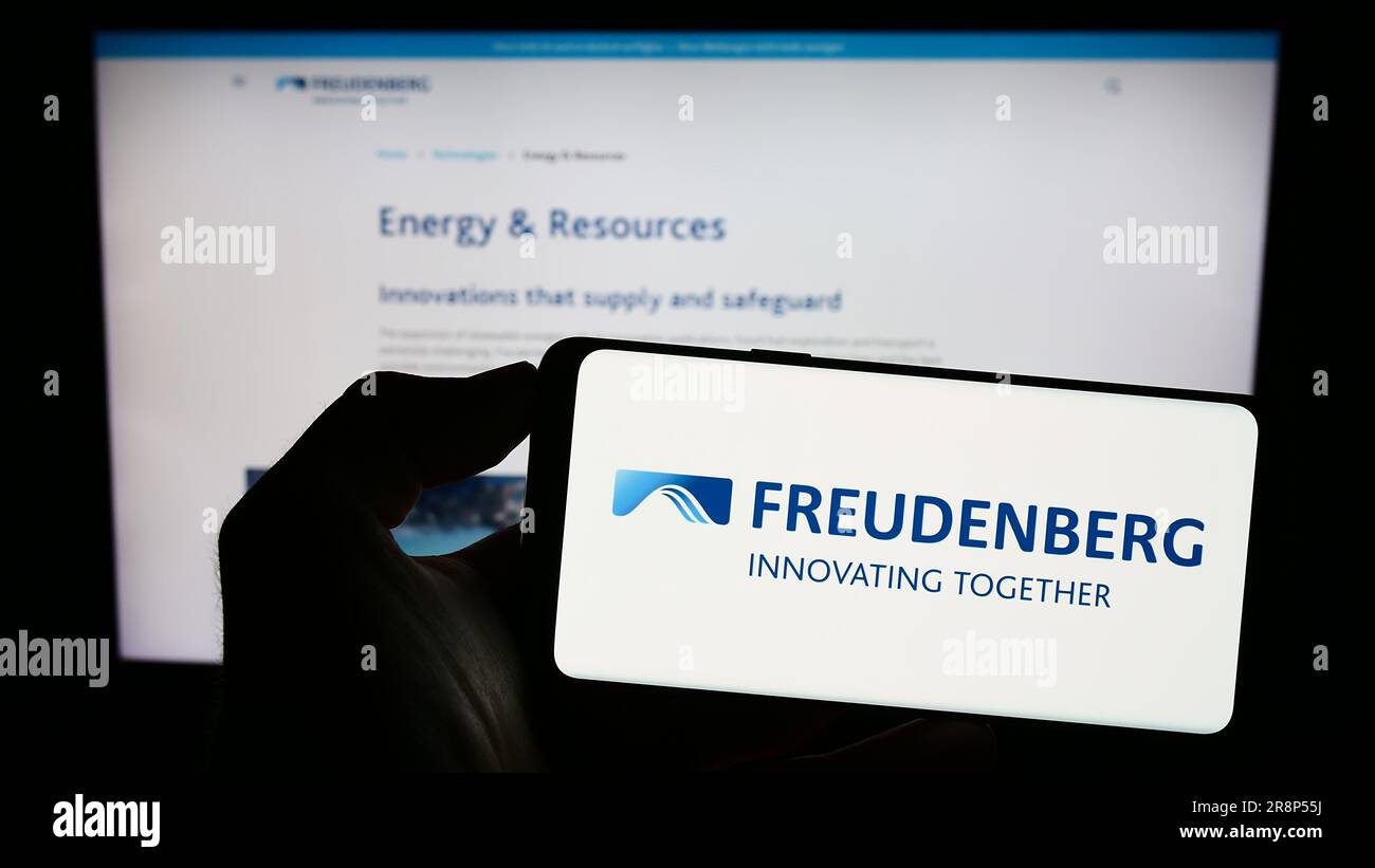 Person holding mobile phone with logo of German company Freudenberg SE ...