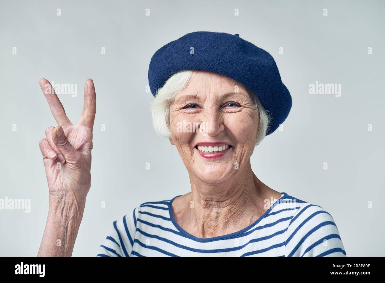Cheerful senior French woman showing two fingers as symbol of greeting ...