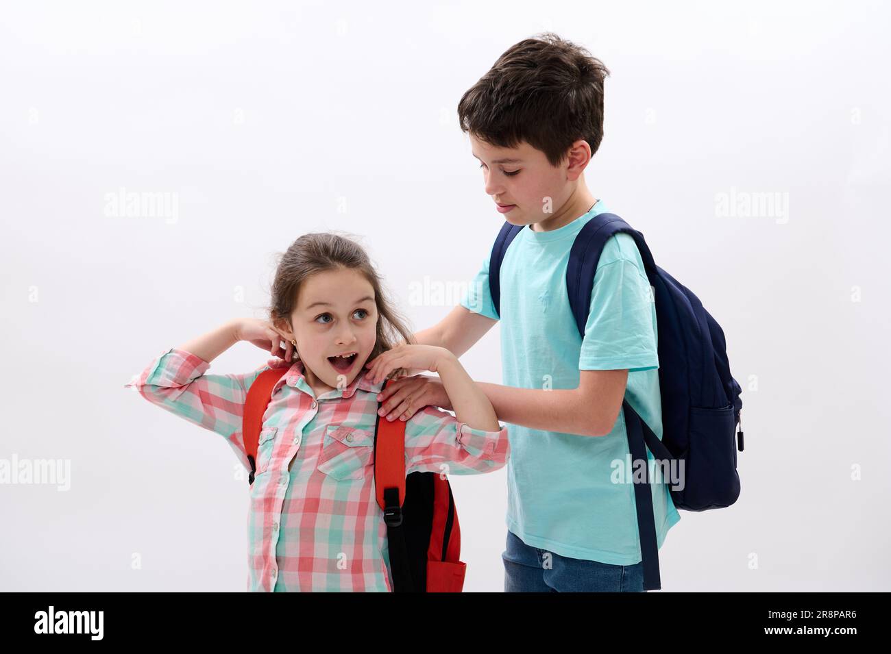 Caring teen boy puts on a backpack on his younger sister back ...