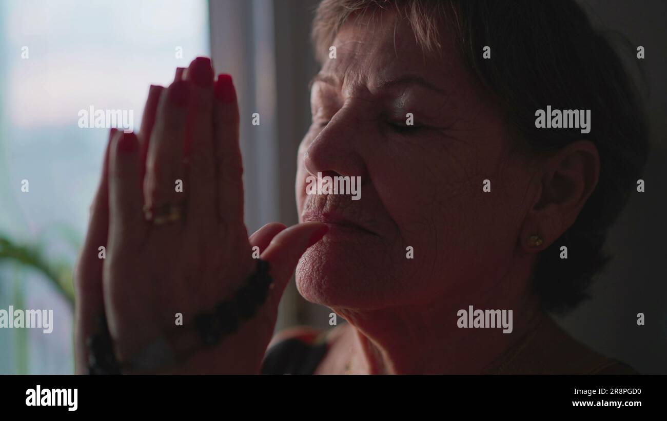 Religious older woman Praying Rosary at home closing eyes in ...