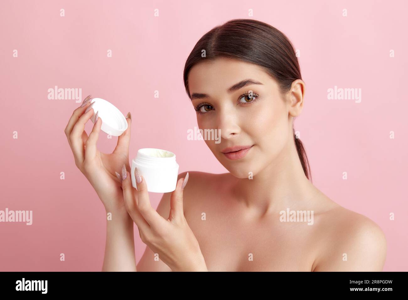Portrait of young beautiful woman posing with face moisturizing cream ...