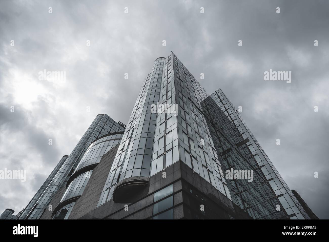 Under the cloudy sky, a modern glassy building stands tall and sleek ...