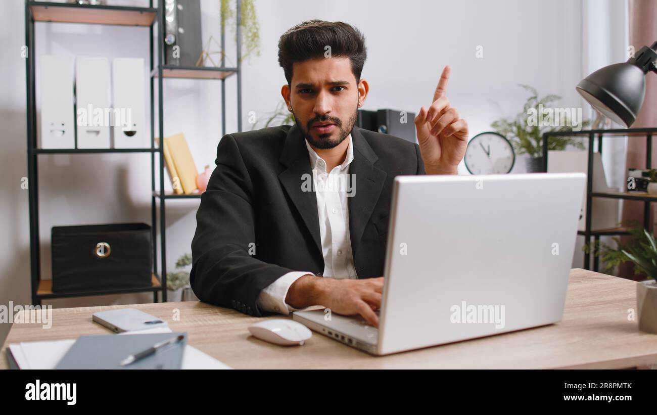 Indian young businessman working on laptop computer shakes finger and ...