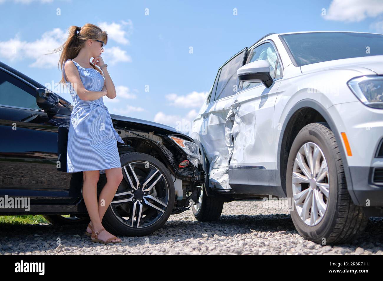 Sad young woman driver standing near her smashed car looking shocked on ...