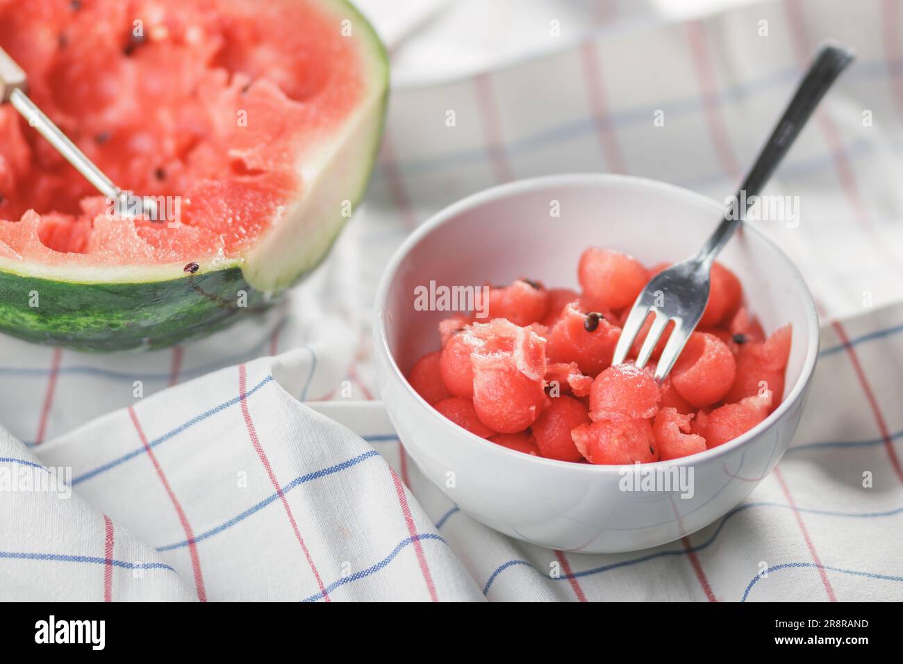 Watermelon balls in a bowl with a dessert fork, next to a hollowed out ...
