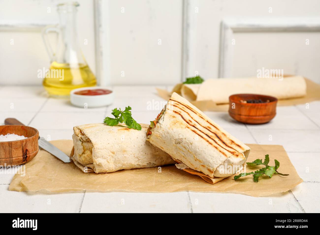 Baking paper with tasty shawarma with parsley on white tile table Stock ...