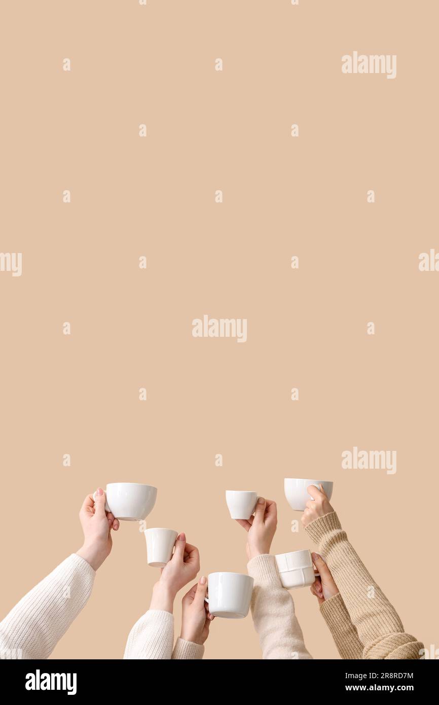 Female hands holding cups on beige background Stock Photo - Alamy