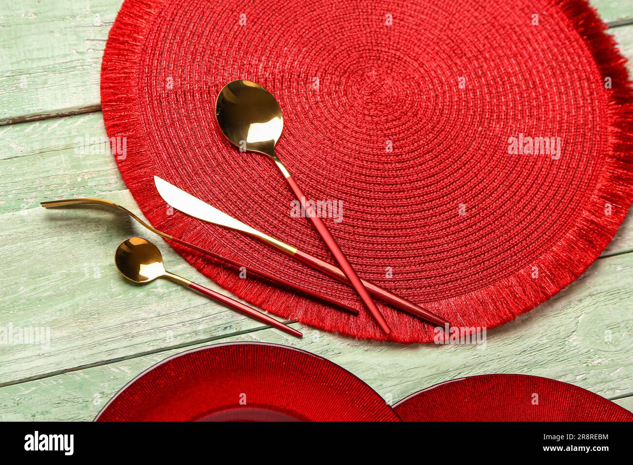 Set of golden cutlery and red place mat on green wooden table, closeup ...