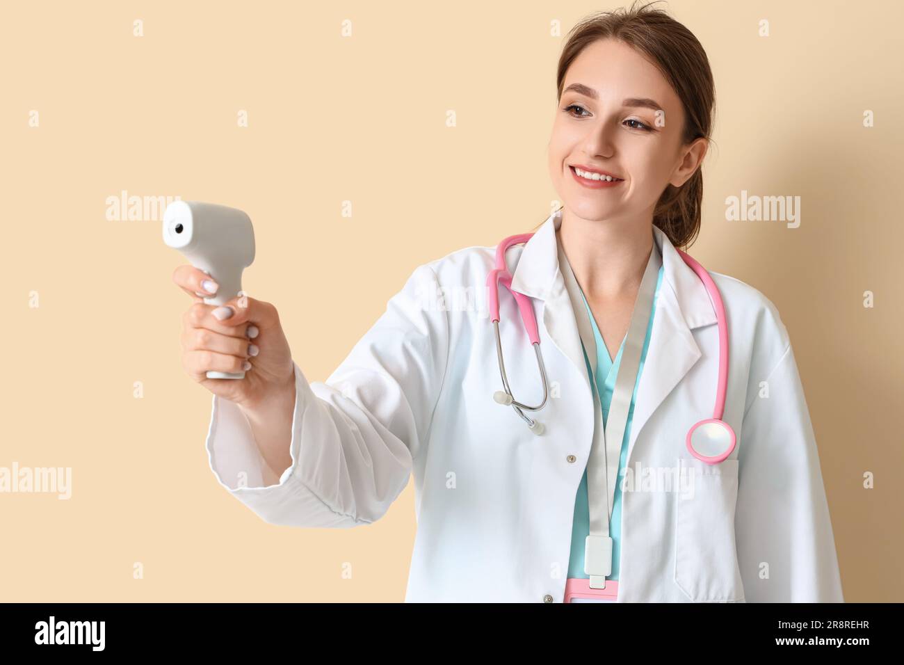 Female medical intern with infrared thermometer on beige background ...