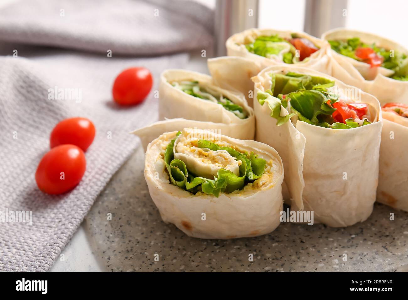 Board of tasty lavash rolls with tomatoes, egg and greens on table ...