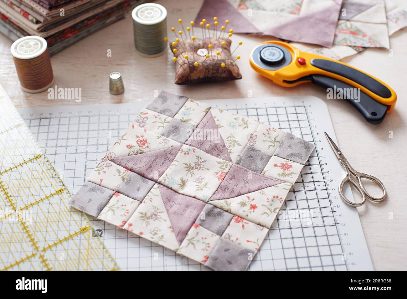 Patchwork block on craft mat, stack of fabric, sewing accessories on ...