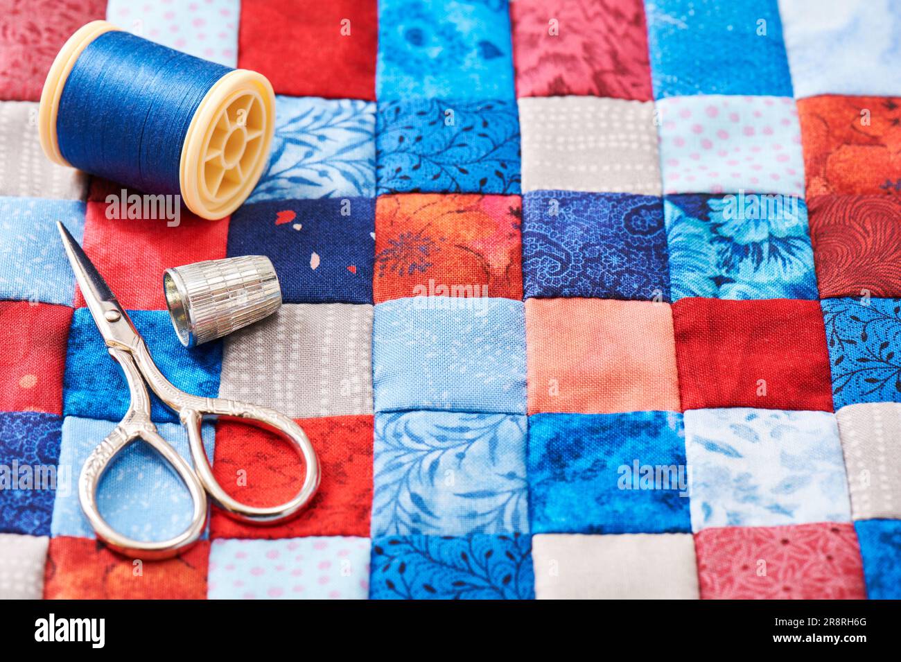 Scissors, thread and thimble lying on blue and red square pieces of ...