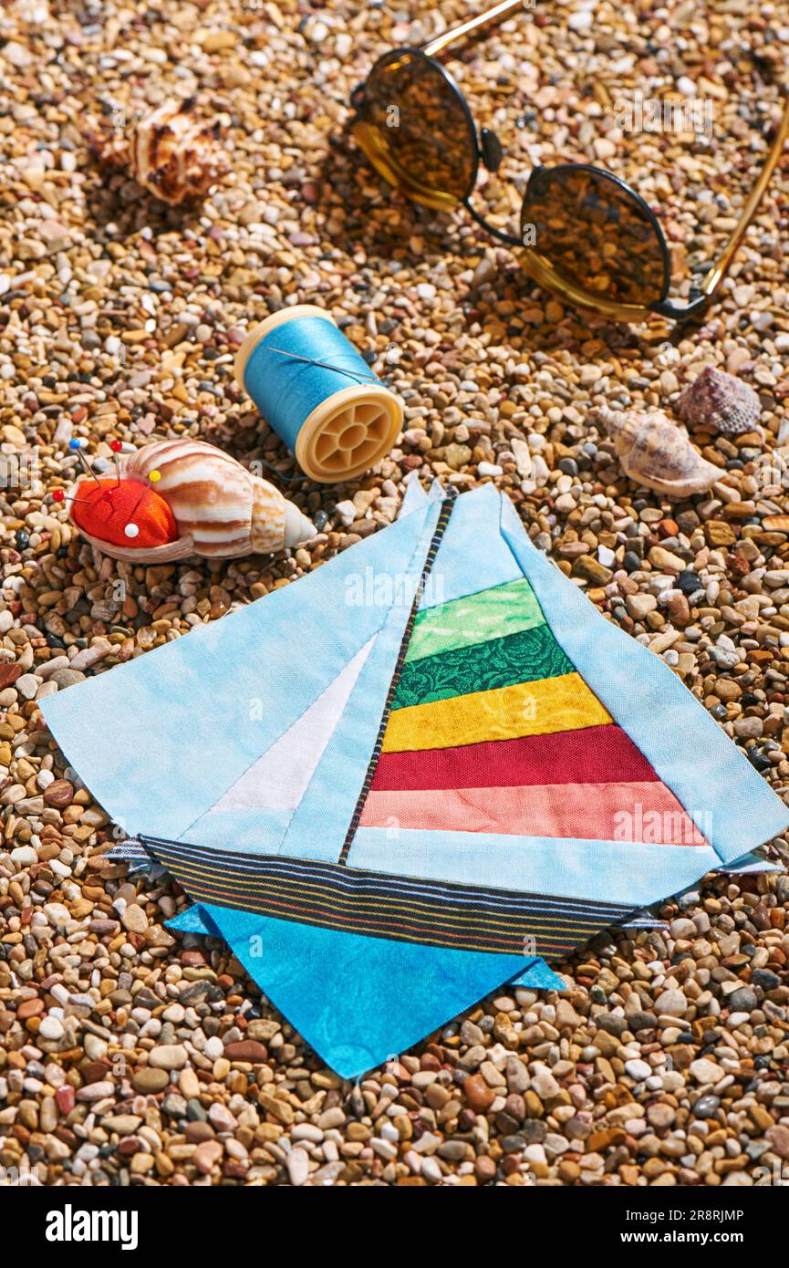 Patchwork block, spool of thread, pin cushion and sunglasses lie on sea stones of beach Stock ...