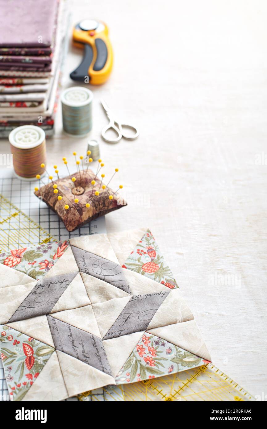 Patchwork block on craft mat, stack of fabric, sewing accessories on ...