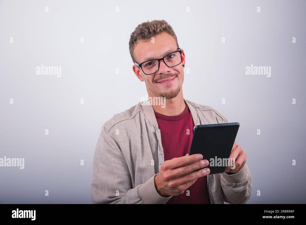 A smiling young man uses his tablet, studio shot with white background ...