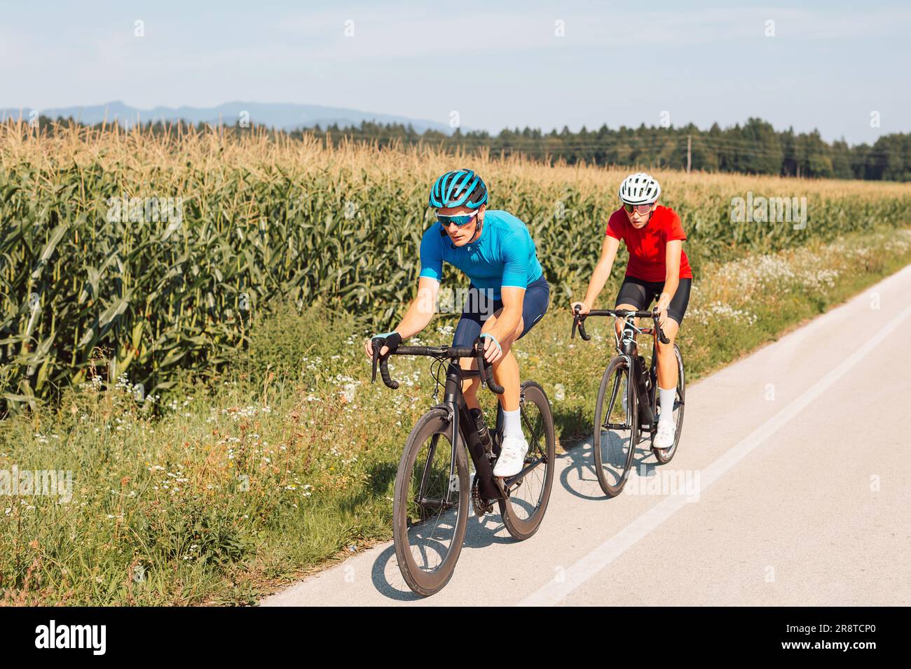 Professional Caucasian racing cyclists couple riding on an asphalt road ...