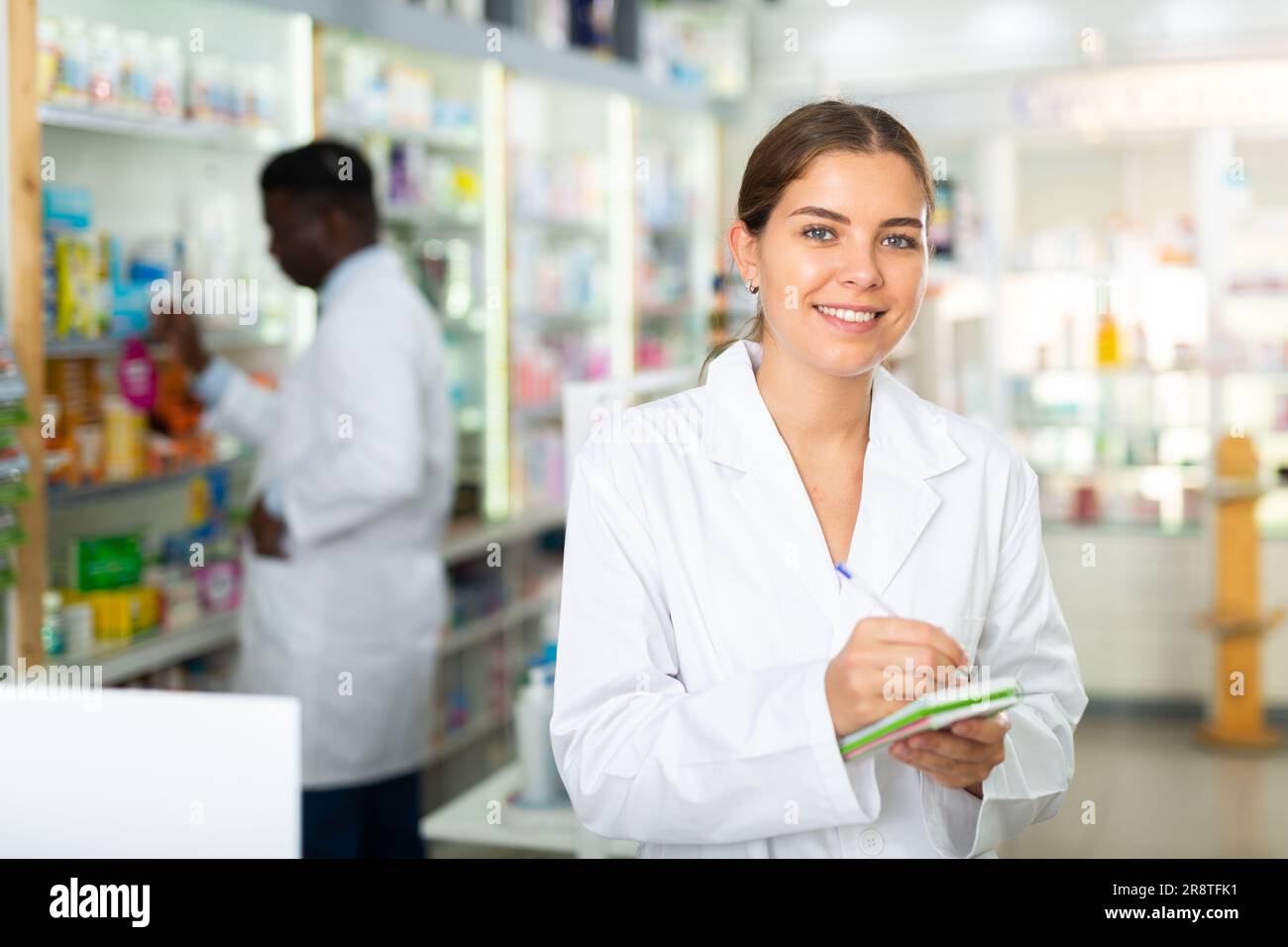 Young smiling female pharmacist making important notes in a notebook ...