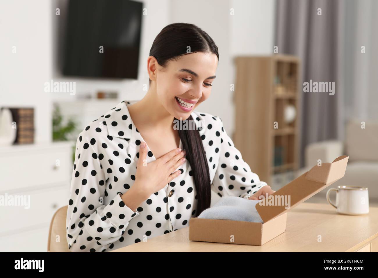 Happy young woman opening parcel at table indoors. Internet shopping ...