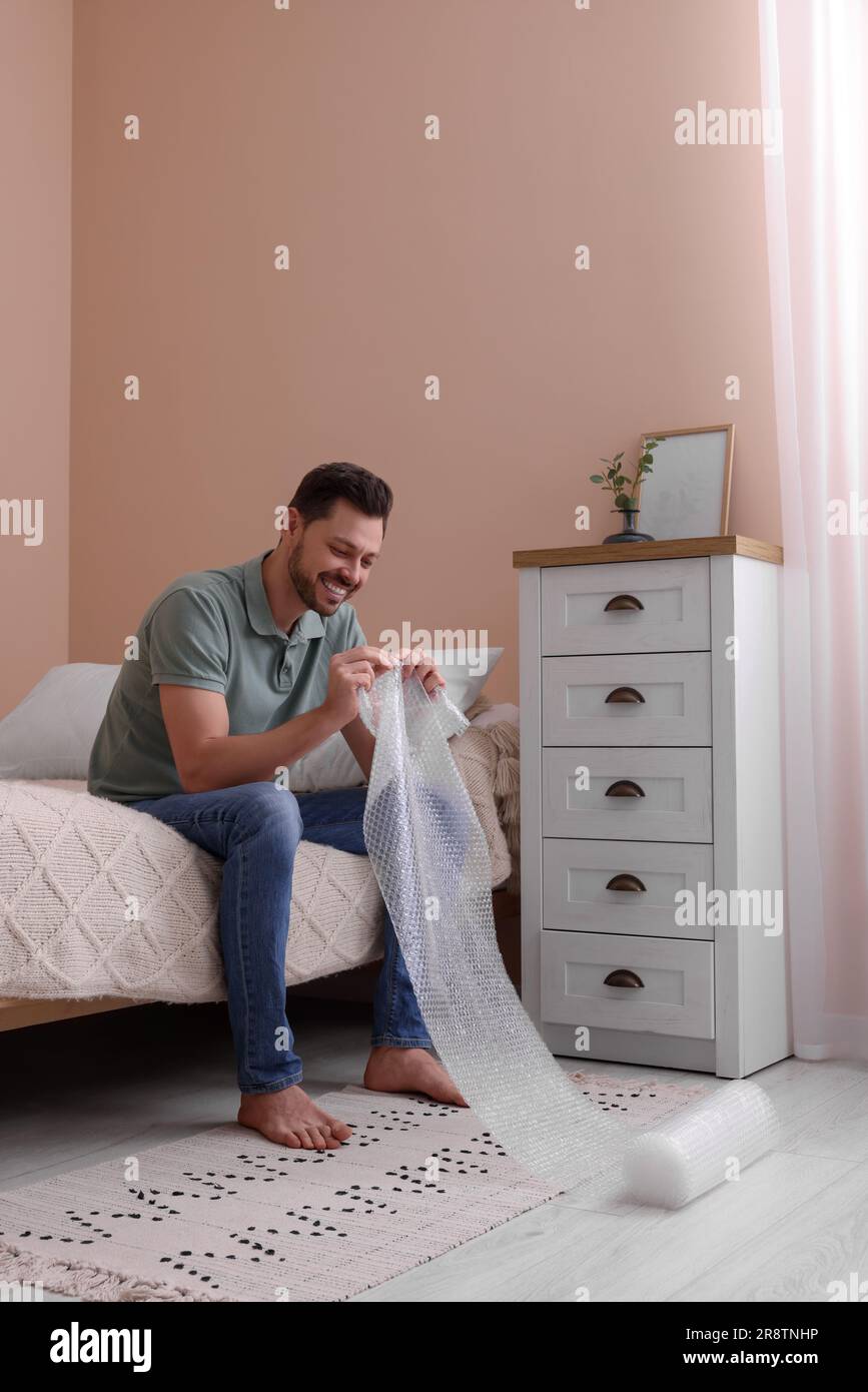 Man popping bubble wrap in bedroom at home. Stress relief Stock Photo ...