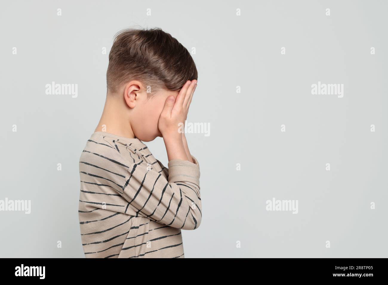 Boy covering face with hands on light grey background, space for text ...