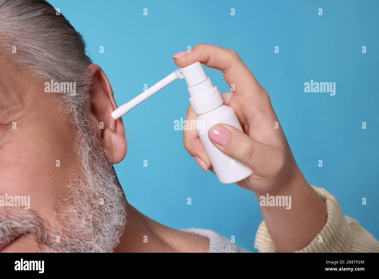 Young woman spraying medication into man's ear on light blue background ...