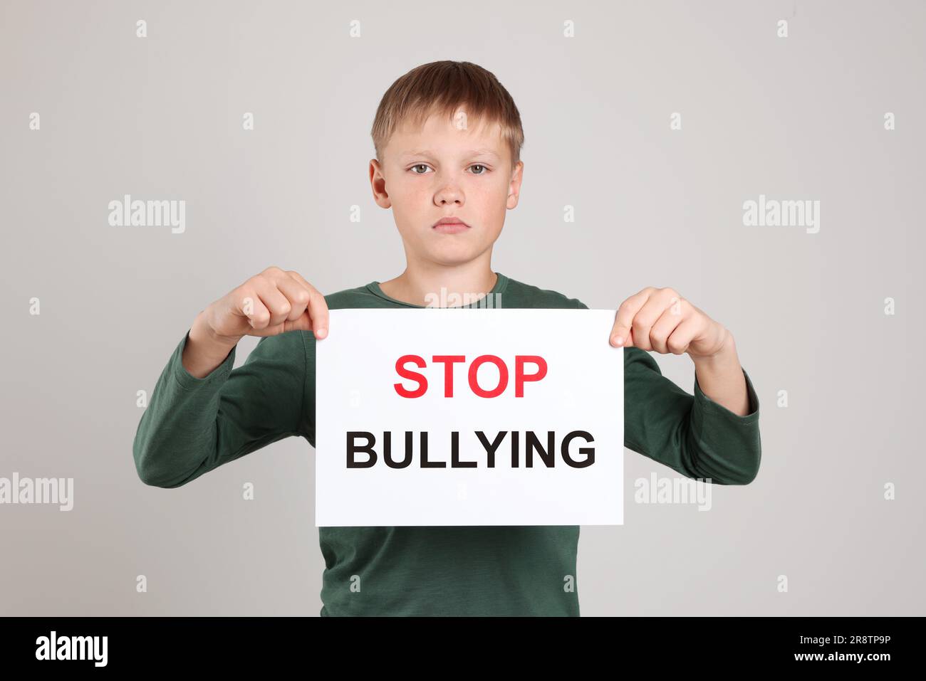Boy holding sign with phrase Stop Bullying on light grey background ...