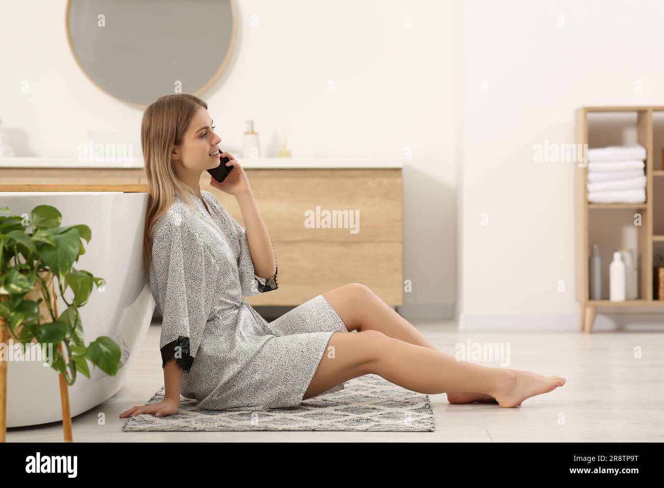 Beautiful happy woman in stylish robe talking on phone in bathroom ...