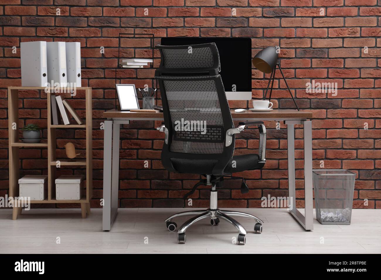 Cosy workspace with computer on desk, chair and bookcase near brick ...