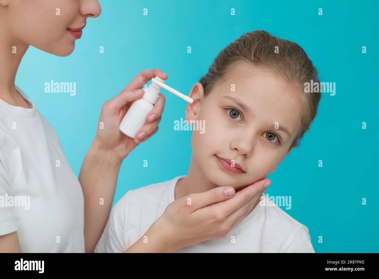 Mother Spraying Medication Into Daughters Ear On Light Blue Background