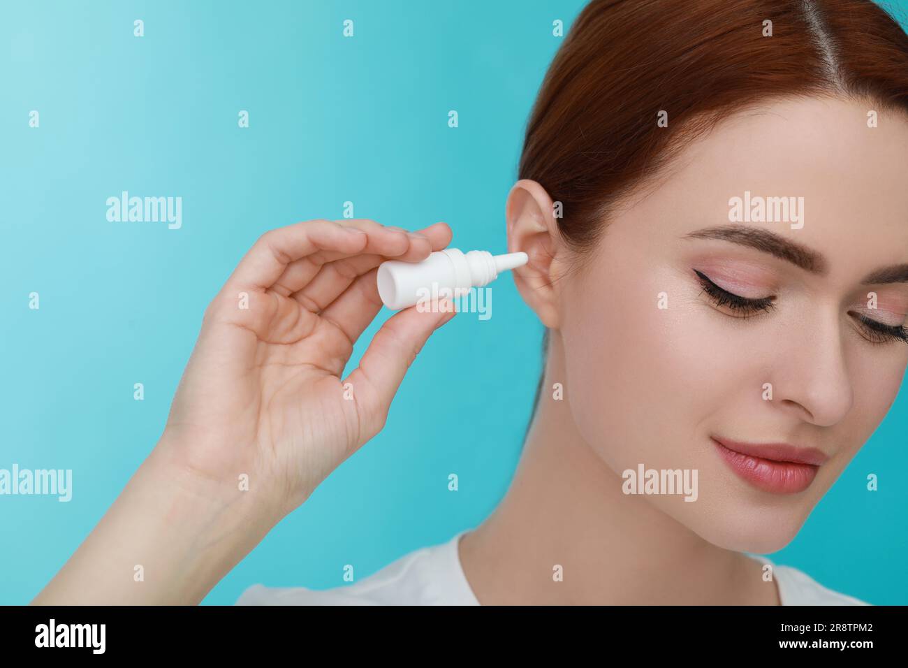 Woman using ear drops on light blue background Stock Photo - Alamy